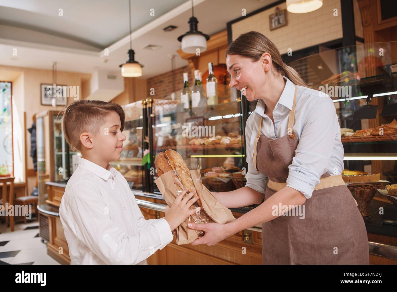 Friendly female baker giving freshly baked bread to her young customer ...