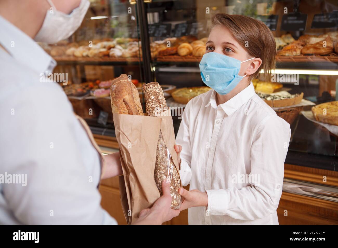 Young boy wearing medical face mask, buying bread at the bakery during ...
