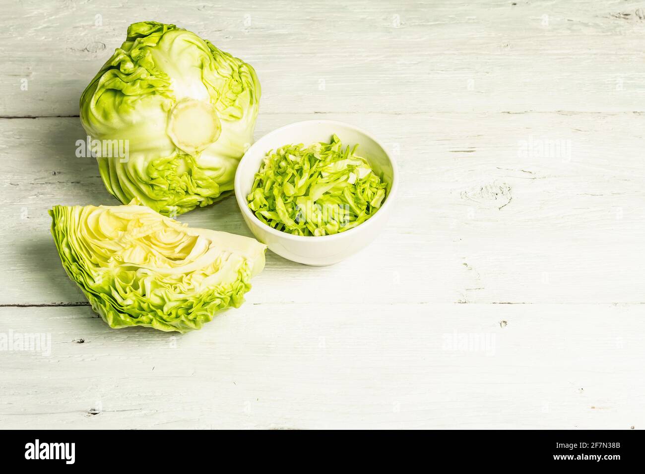 Fresh young shredded cabbage, whole head and cut piece on white wooden ...