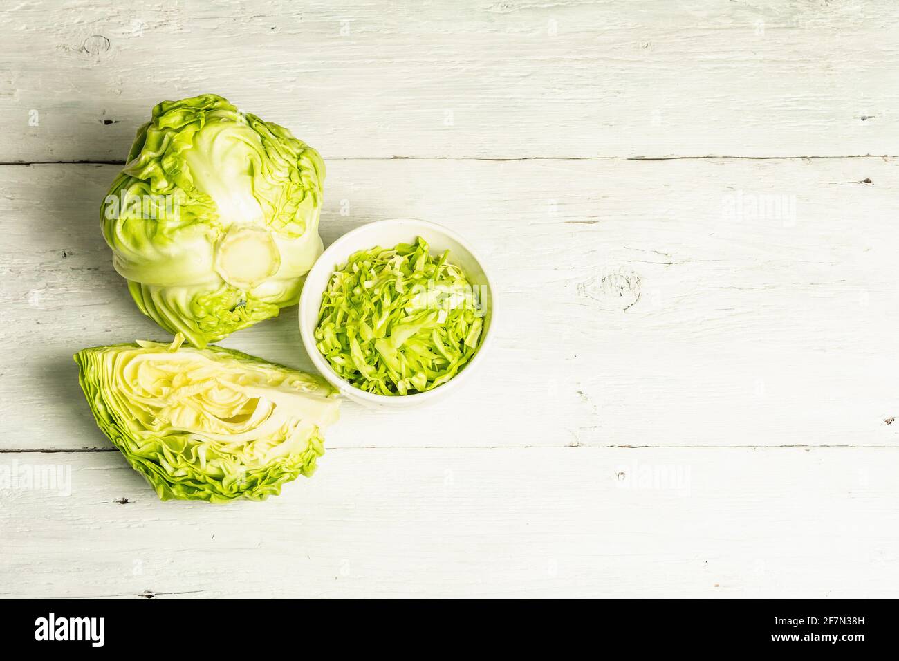 Fresh young shredded cabbage, whole head and cut piece on white wooden ...