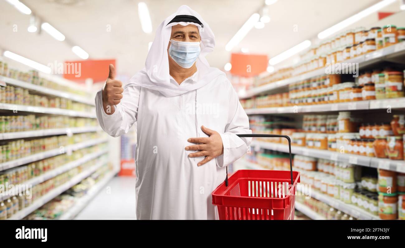 Arab man with a face mask gesturing thumbs up and holding a shopping ...