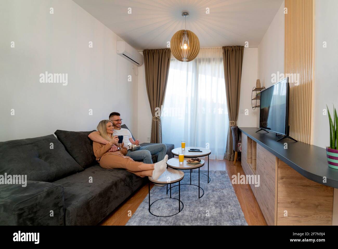 A young couple in an embrace watching TV in a semi-sitting position on ...