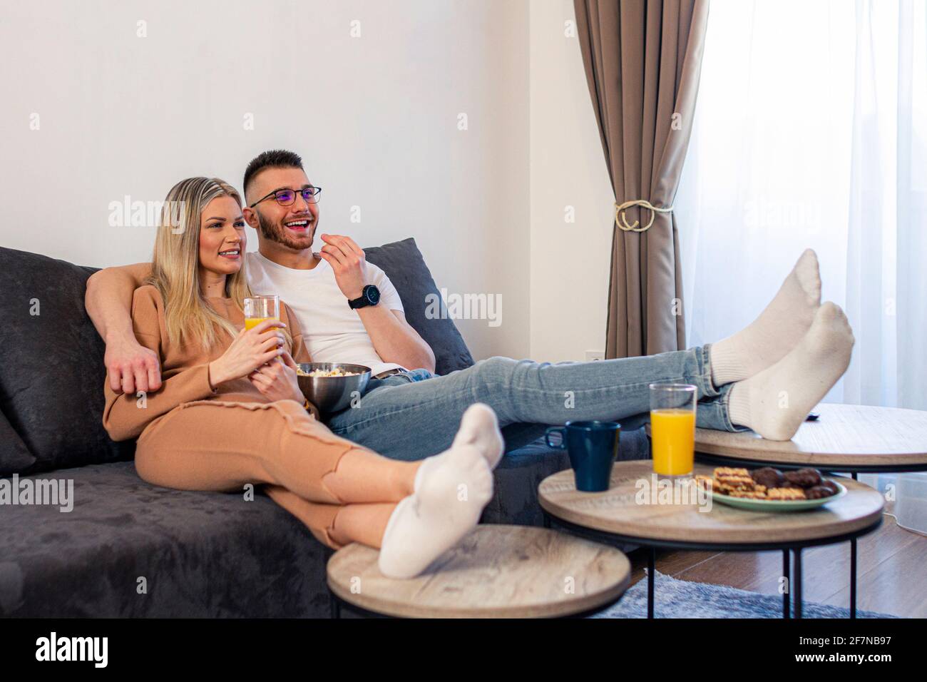 A young couple in an embrace watching TV in a semi-sitting position on ...