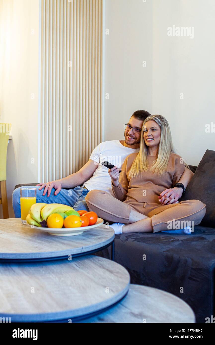 A young couple in an embrace watching TV in a semi-sitting position on ...