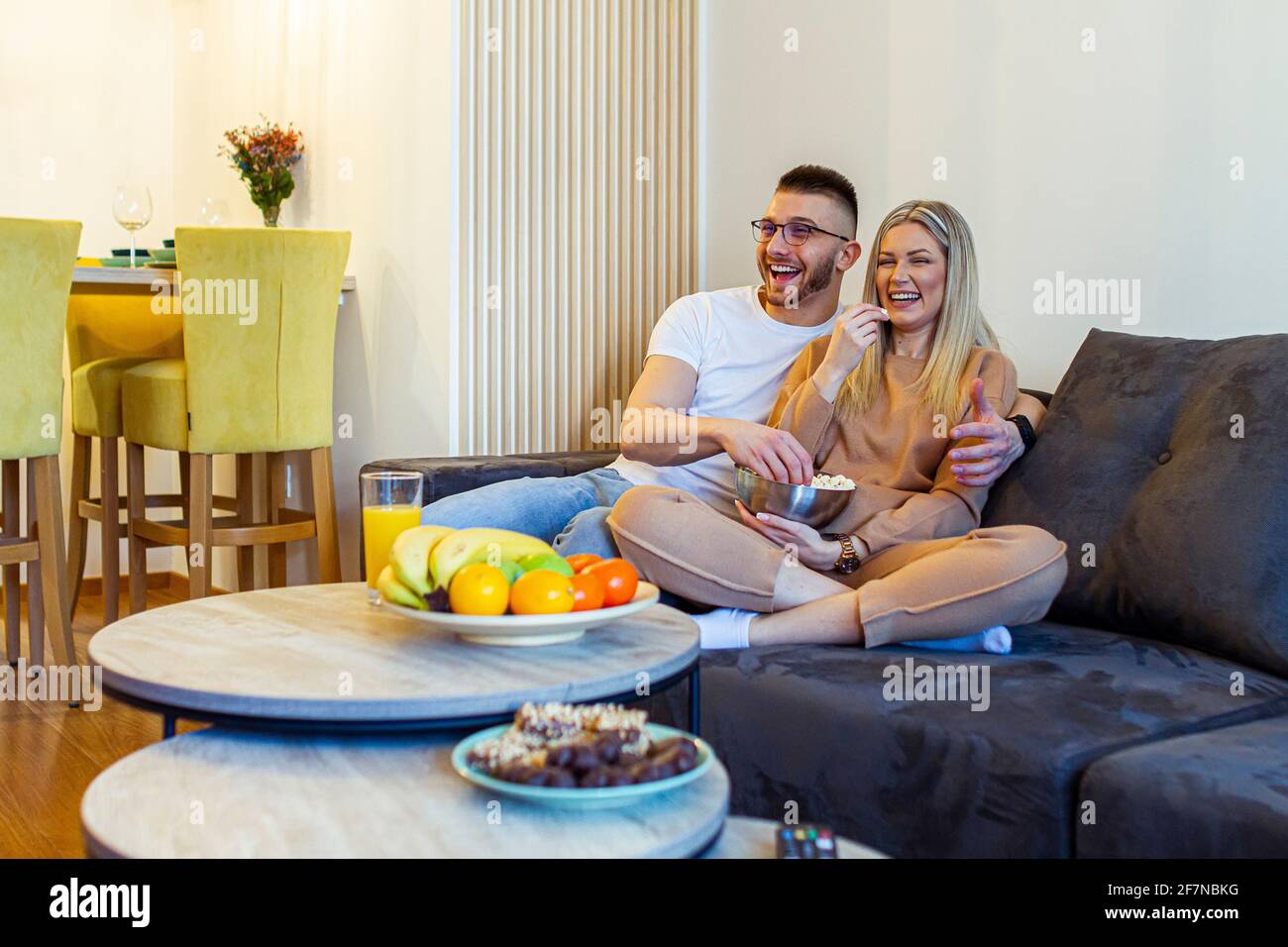 A young couple in an embrace watching TV in a semi-sitting position on ...