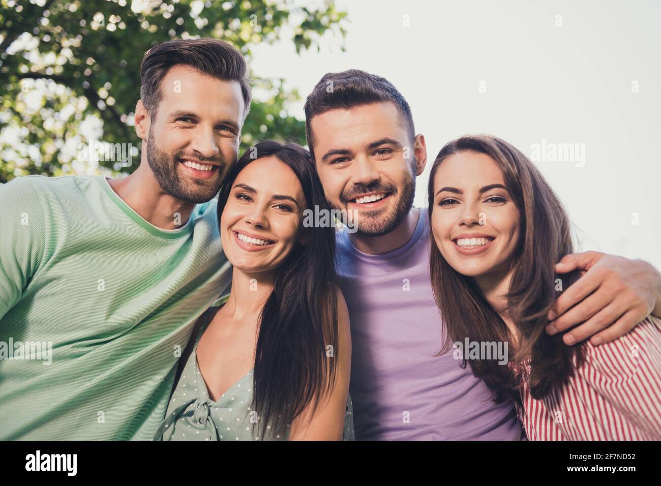 Low angle view photo of four happy friends men and women hug beaming ...