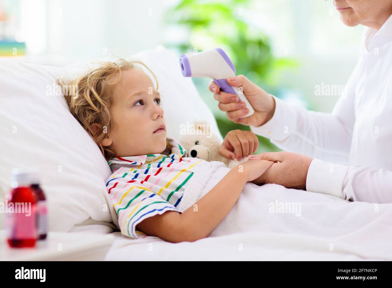 Sick little boy with medicine. Mother checking fever of ill child in bed. Unwell kid with ...