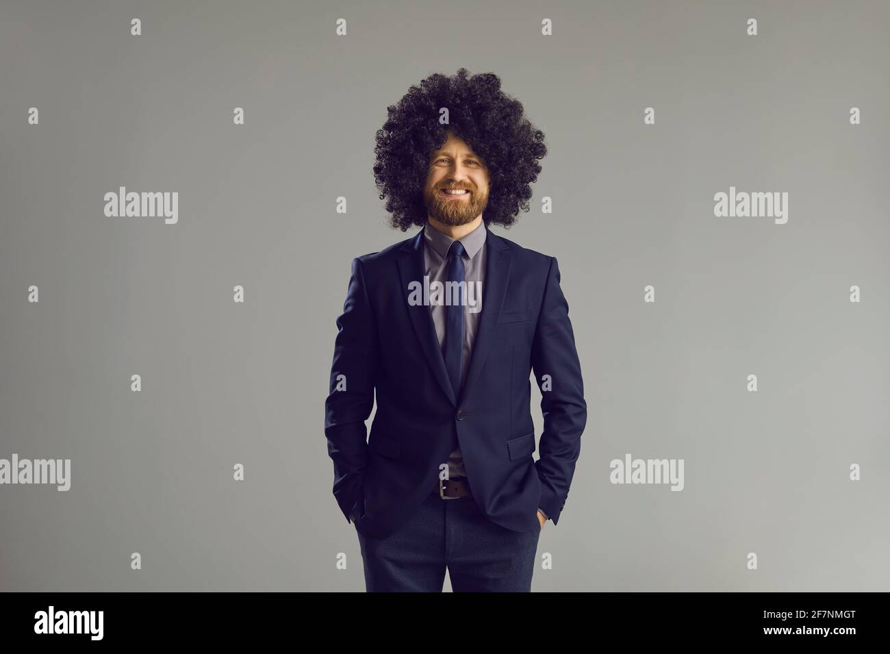 Happy guy in elegant suit and crazy curly wig standing hands in pockets ...