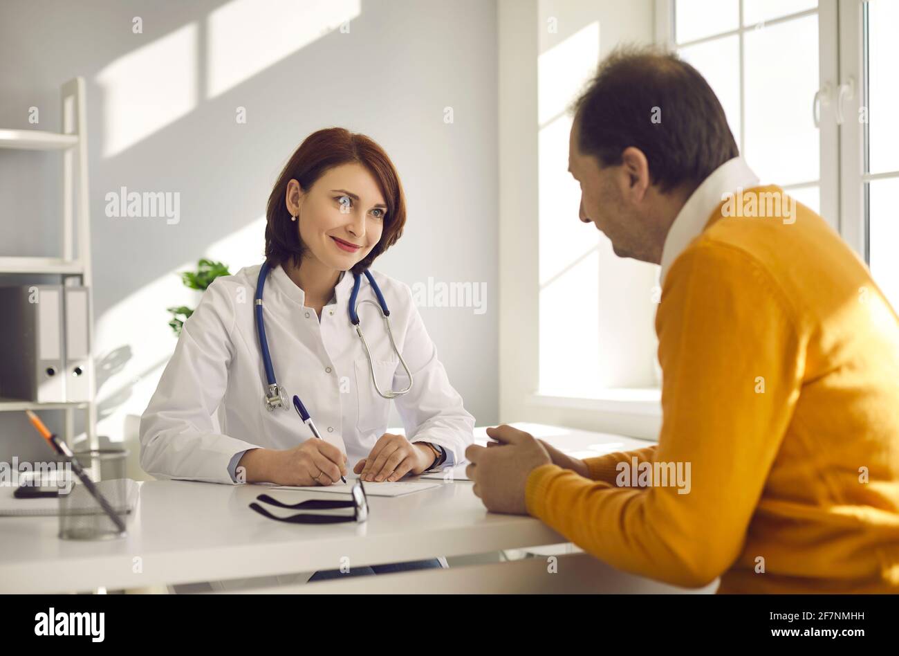 Happy friendly doctor sitting at her desk, looking at her senior ...