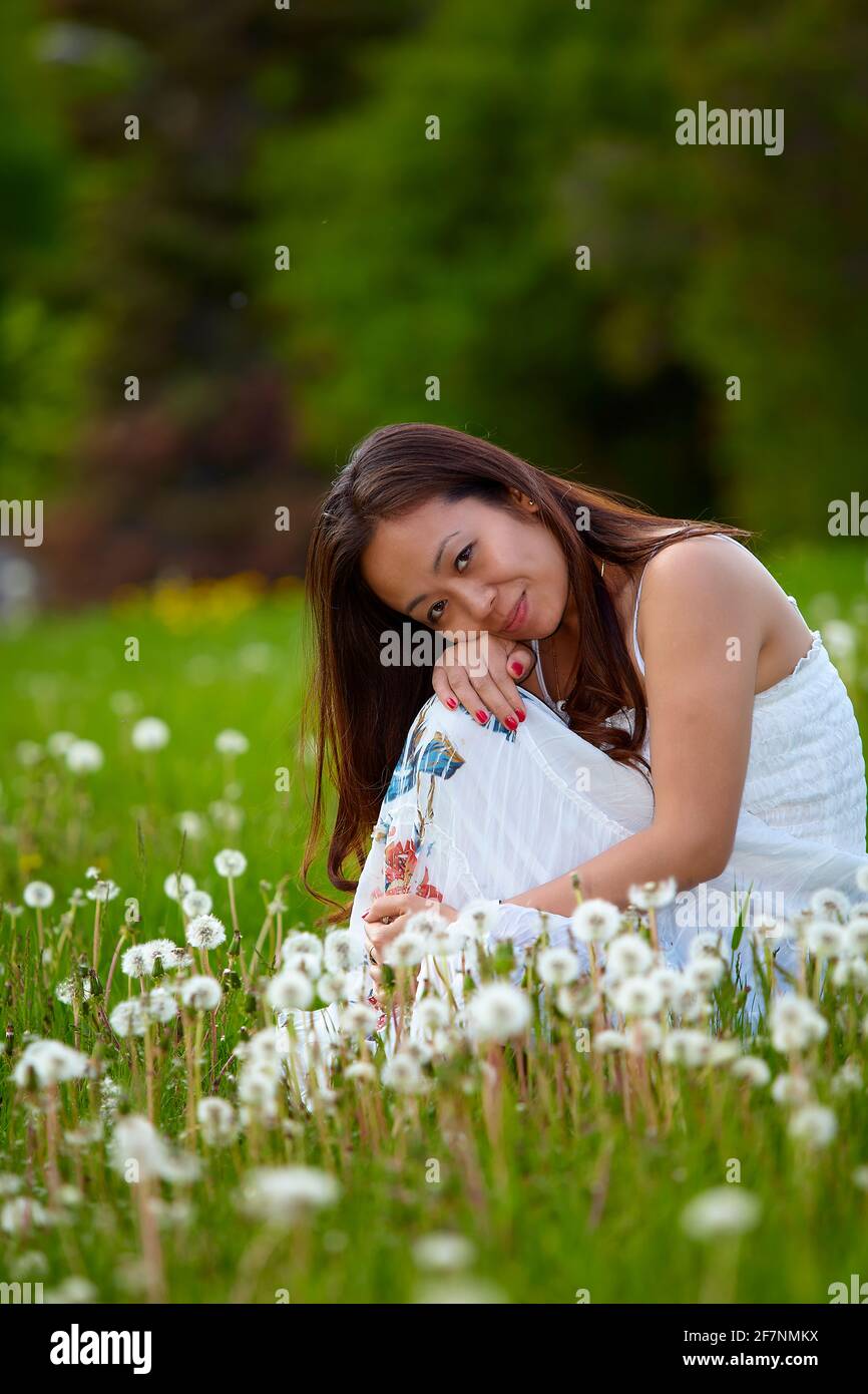 Side view of filipino female sitting on grass in a field of dandelions ...