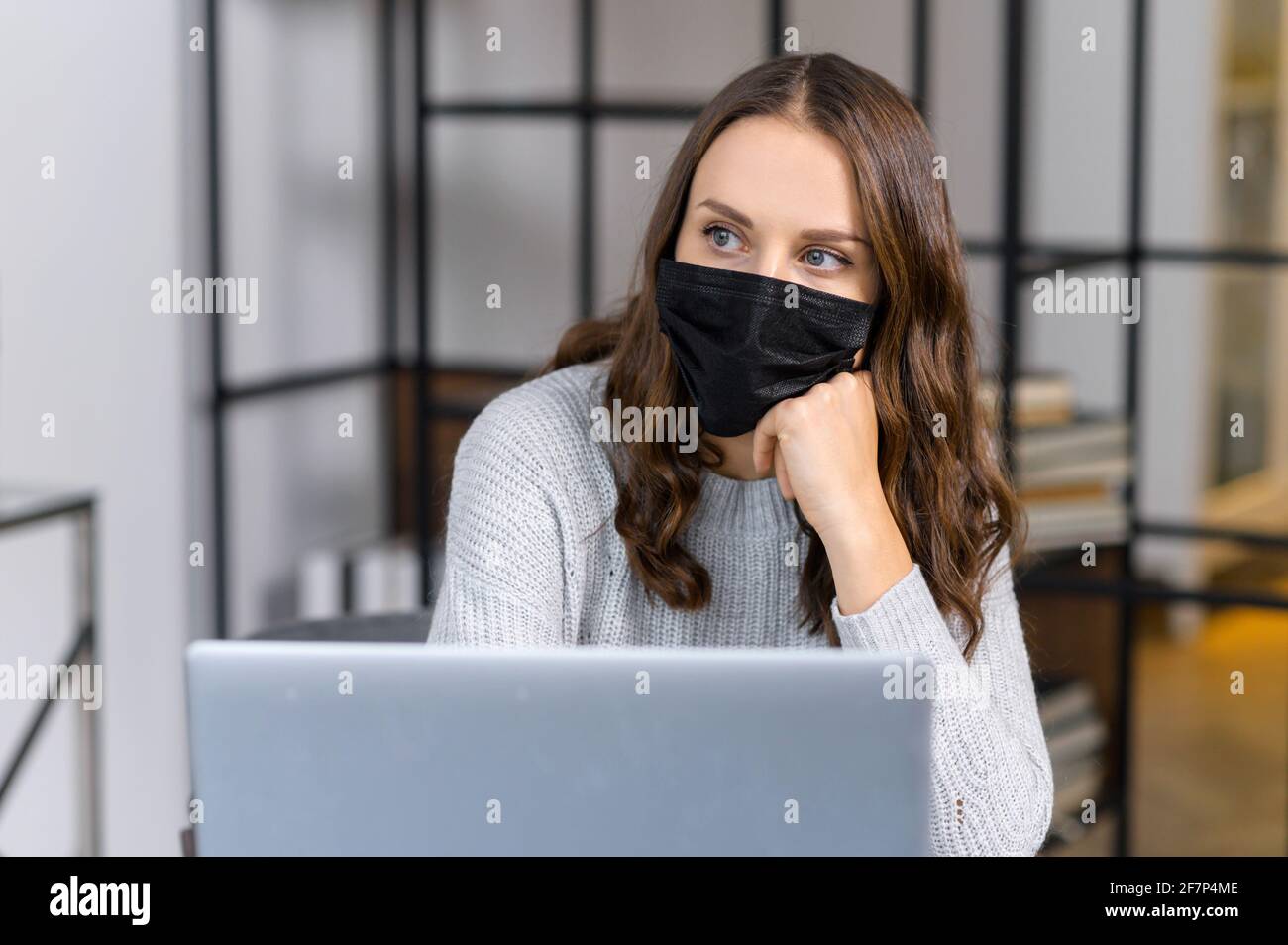 Pensive young businesswoman wearing protective medical mask sitting on ...