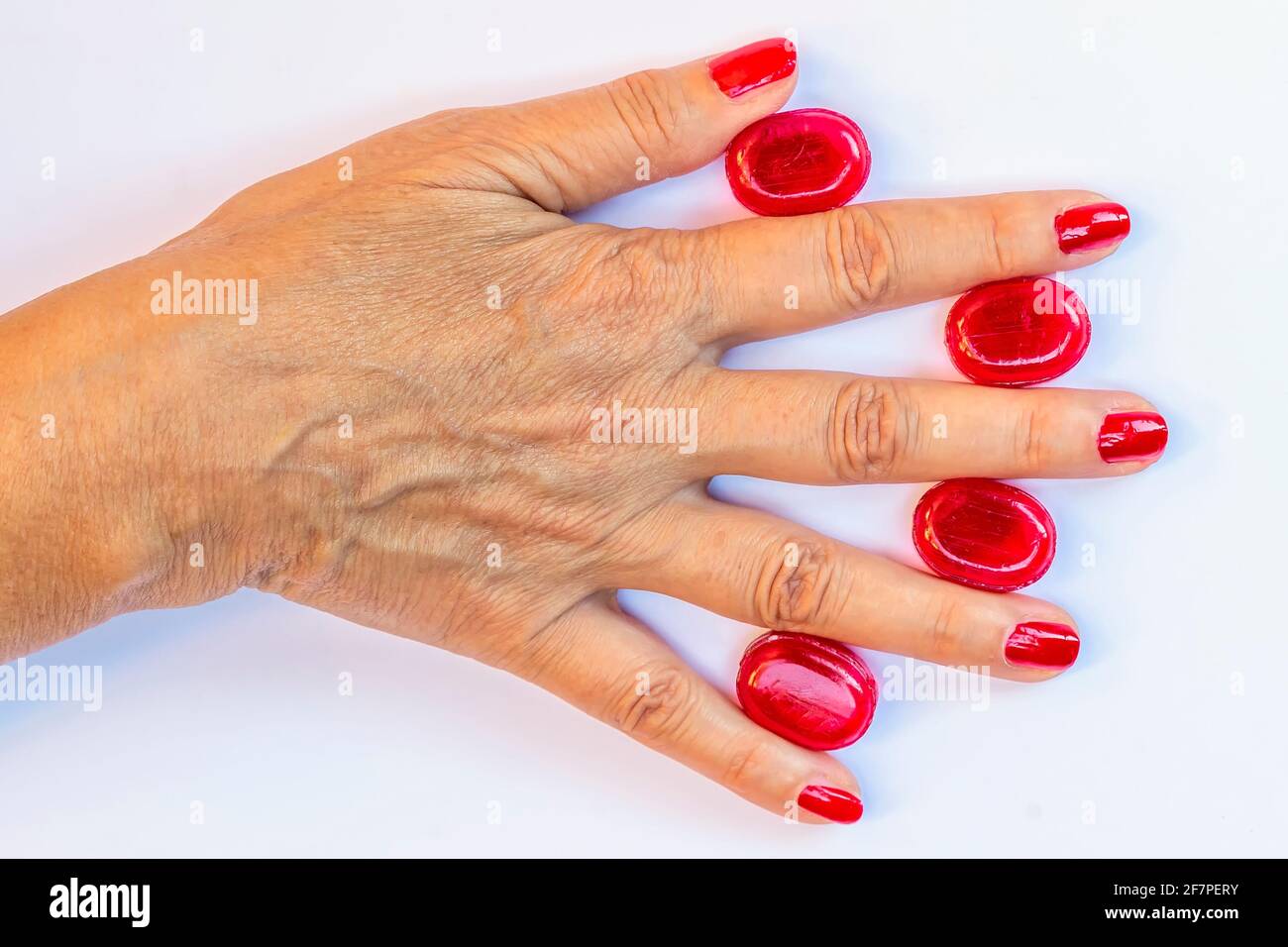 The back of a female hand rests on a white surface with red candies ...