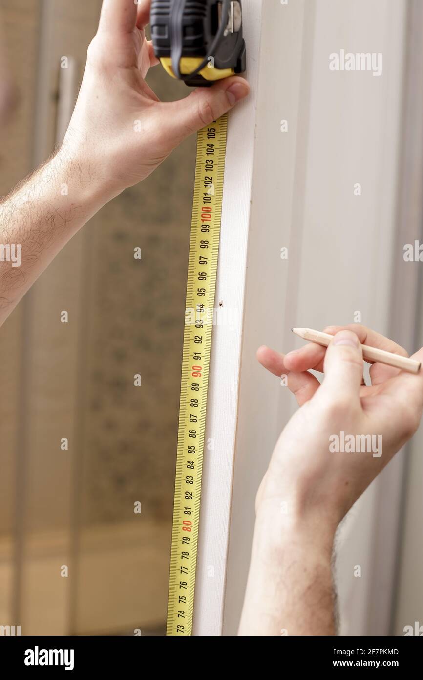 Carpenter hands take measurements on a wooden door with a joiner tape ...