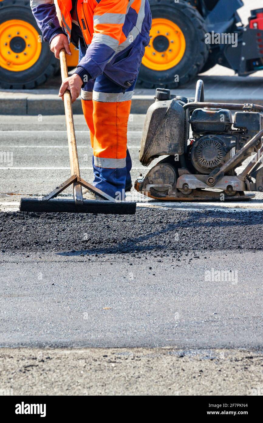 A road worker repairs a section of road with a wooden level in front of ...