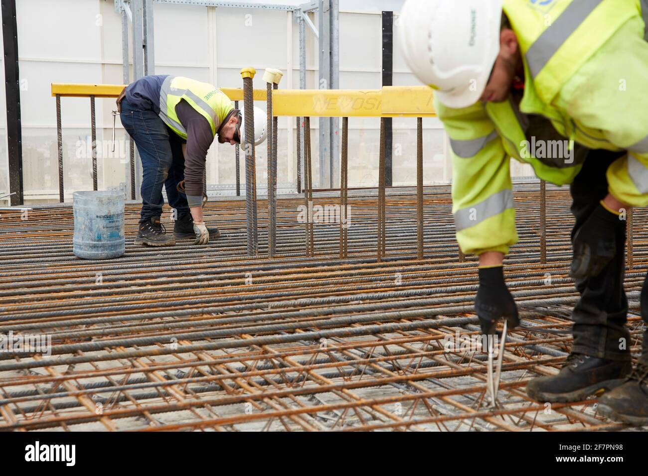 Construction workers bind steel mesh together with plyer in preparation ...