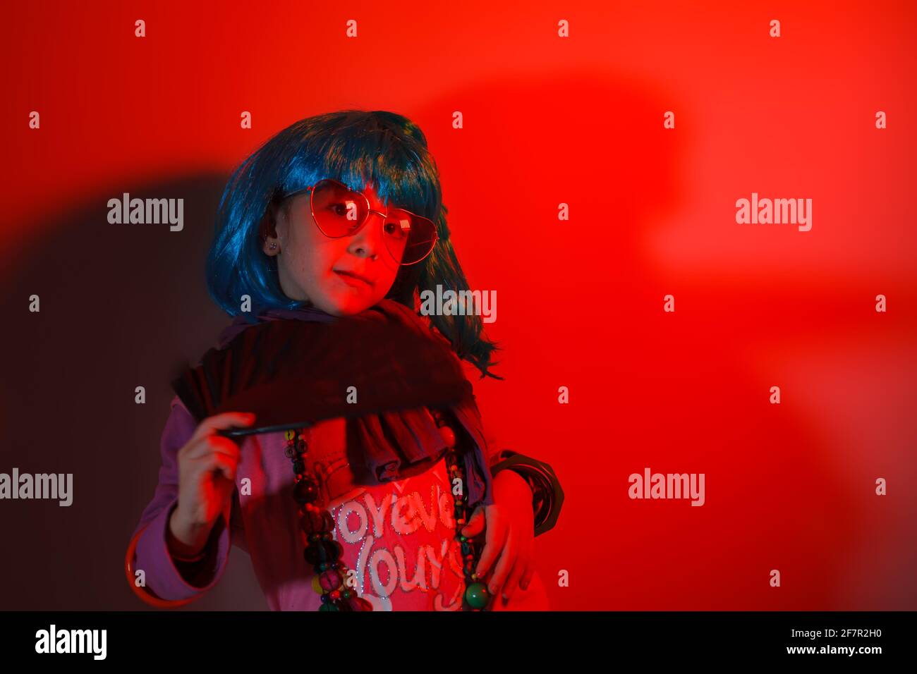 Little girl posing with a fan for a photo shoot on a red background ...