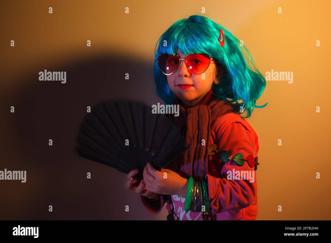 Little girl posing with a fan for a photo shoot on a beige background ...