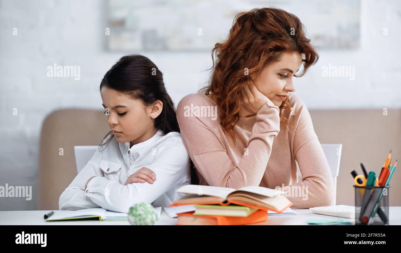 Sad mother and daughter sitting near books on blurred foreground Stock ...