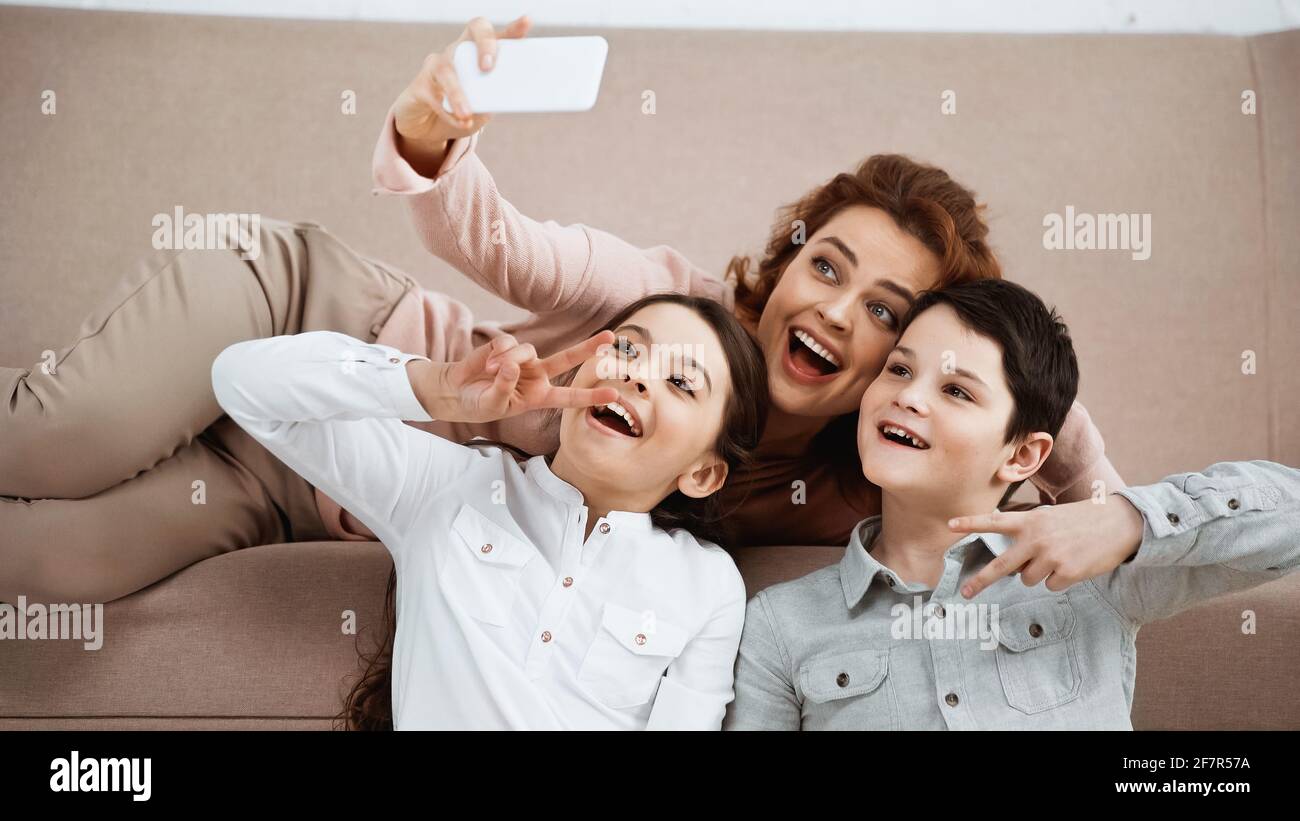 Cheerful family showing peace sign while taking selfie on couch Stock ...