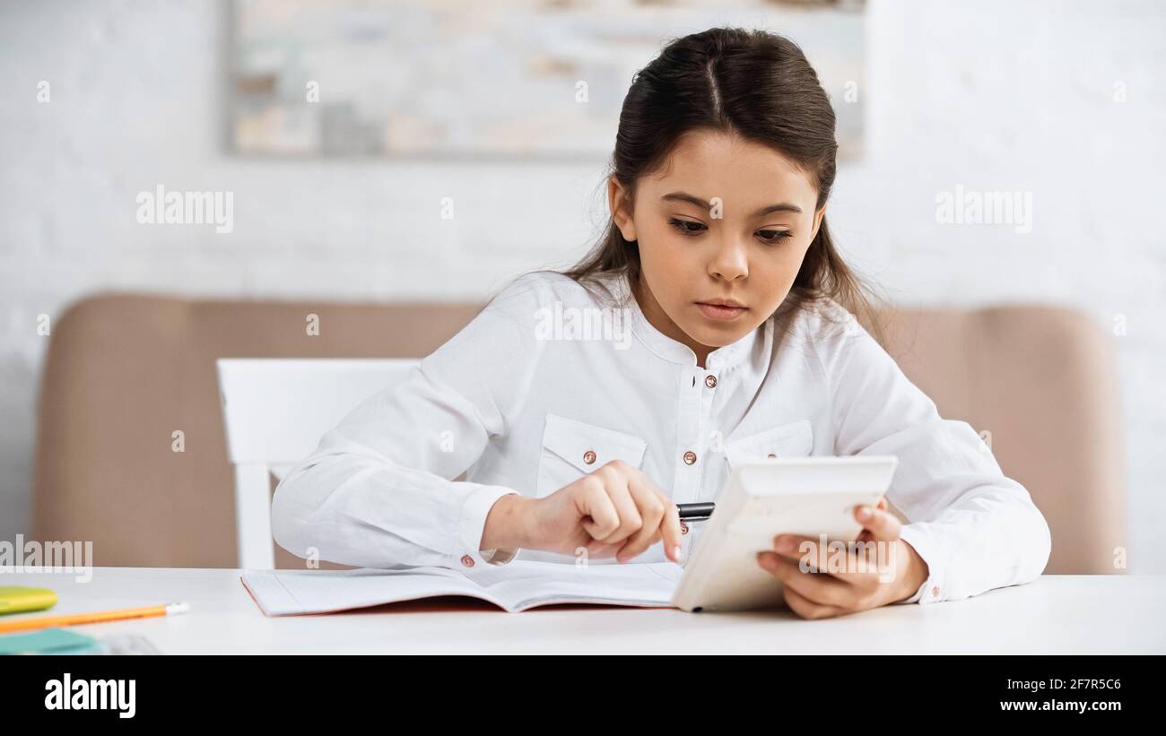Preteen girl using calculator near notebook and stationery at home ...