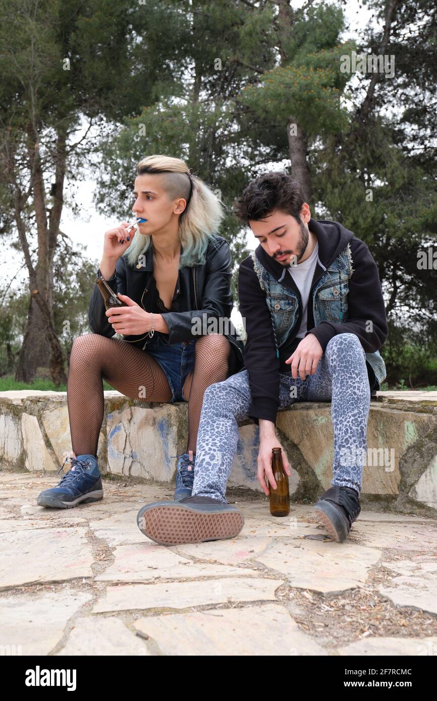 Young punk couple smoking and drinking beer in a park. Rock and roll ...