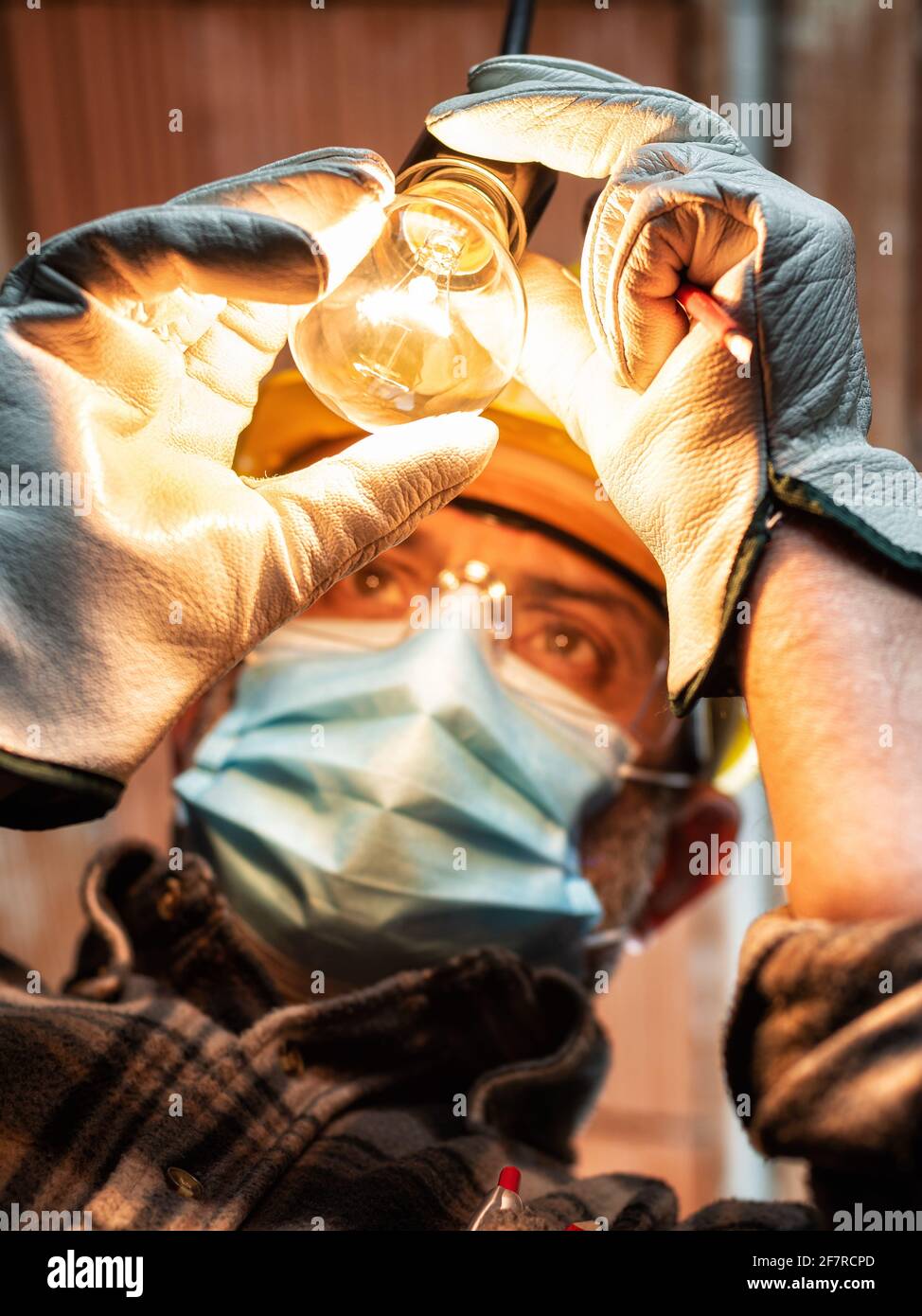 Electrician worker at work replaces the light bulb protected by helmet ...