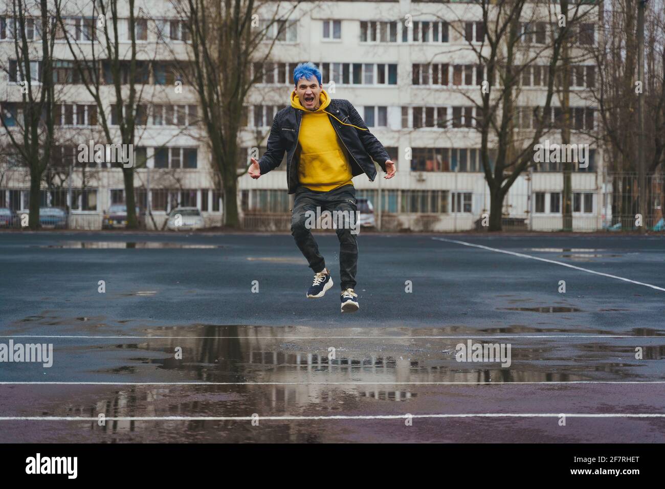 Young man jumps in puddle on sports stadium on background of high-rise ...