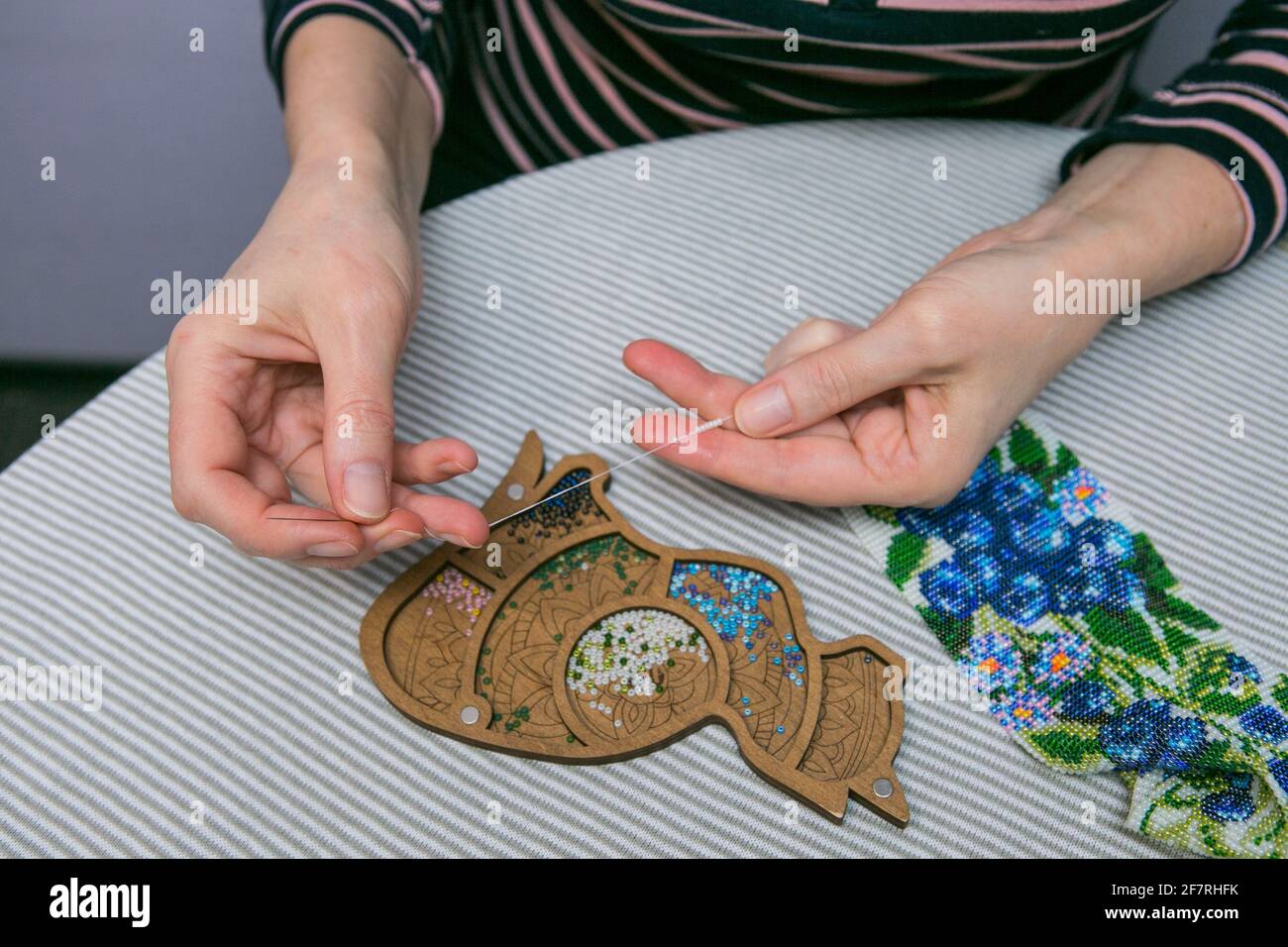Weaving from beads. Close-up - a woman's hands are stringing beads on a ...