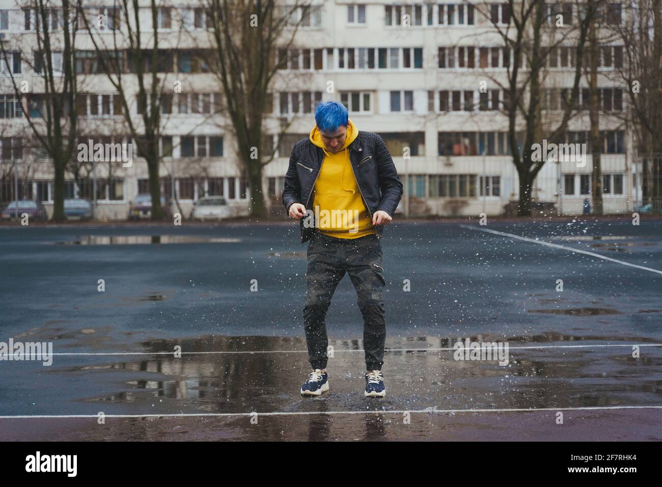 Young man jumps in puddle on sports stadium on background of high-rise ...