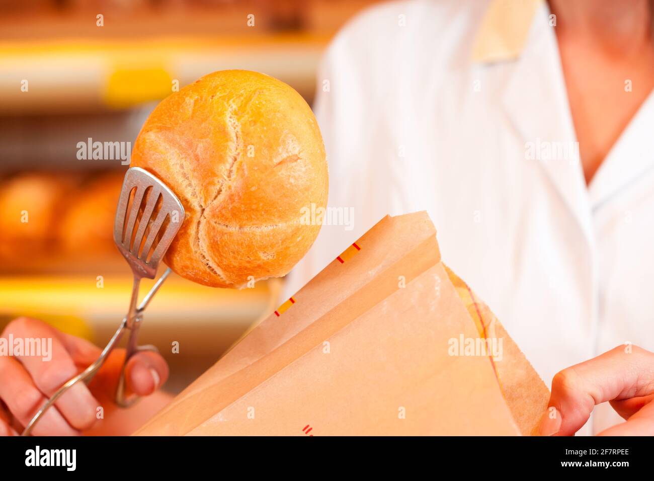 Salesperson in a bakery is packing bread for a customer in a bag, close ...