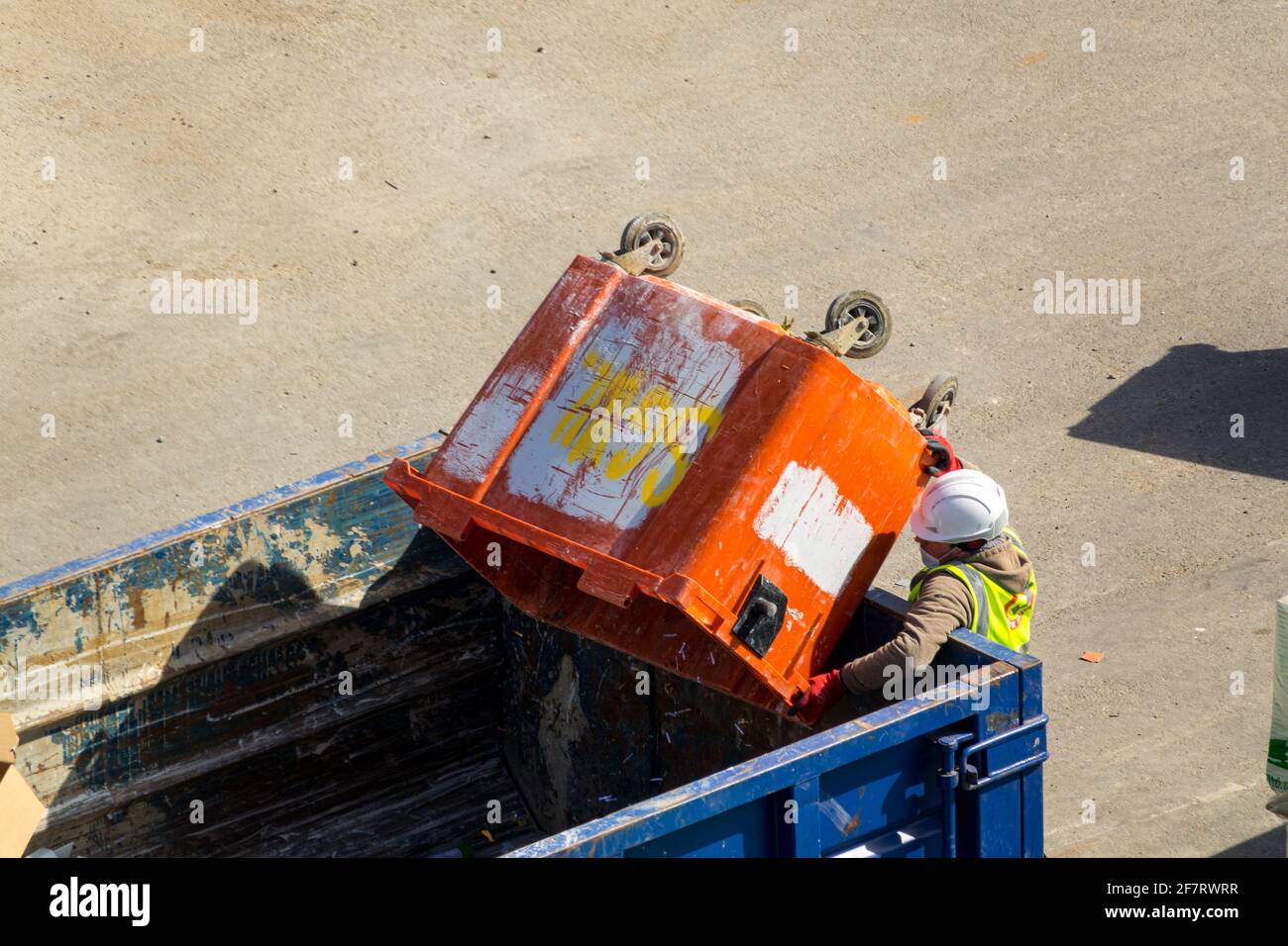 Construction worker disposing of debris into a skip on a building site ...