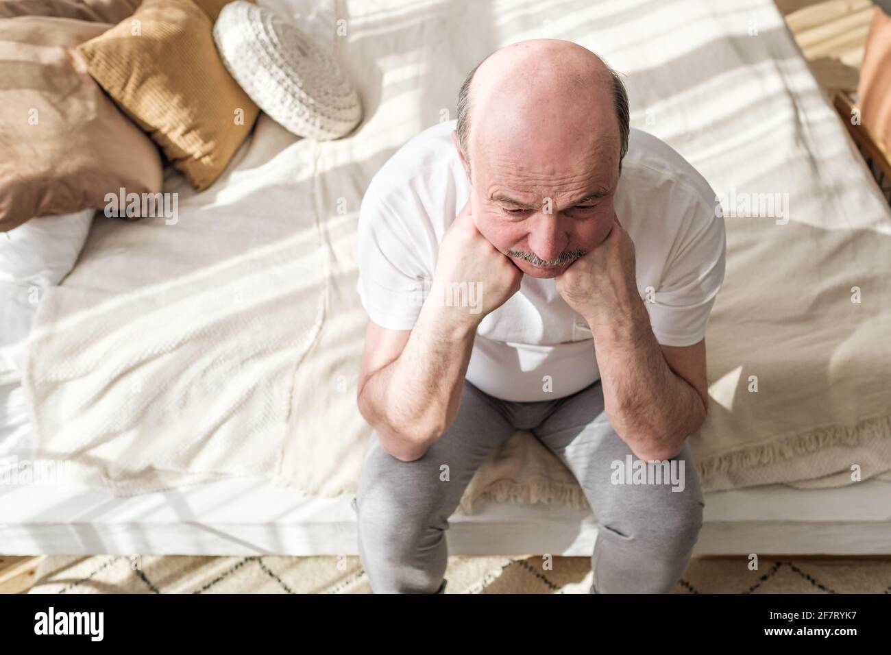 Sad caucasian man sitting alone on his bed with his head on his hand ...