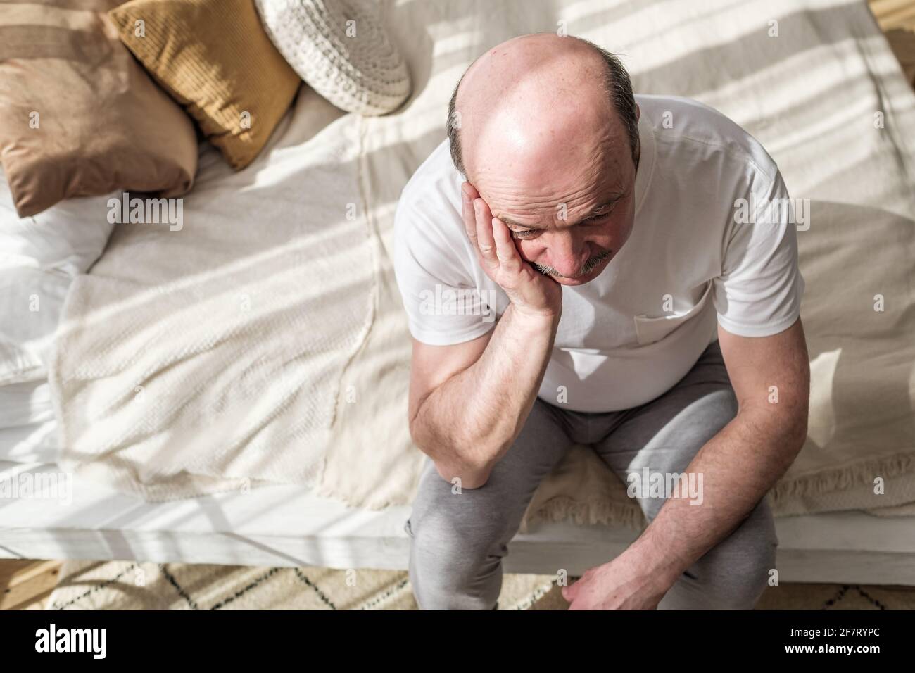 Sad caucasian man sitting alone on his bed with his head on his hand ...