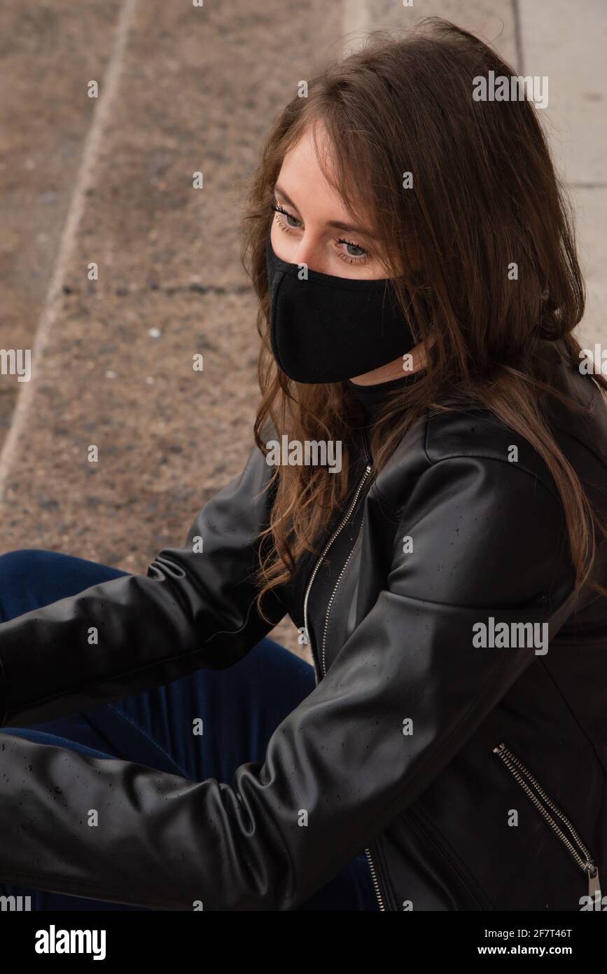 Vertical shot of a Spanish female in black wearing a face mask outdoors ...