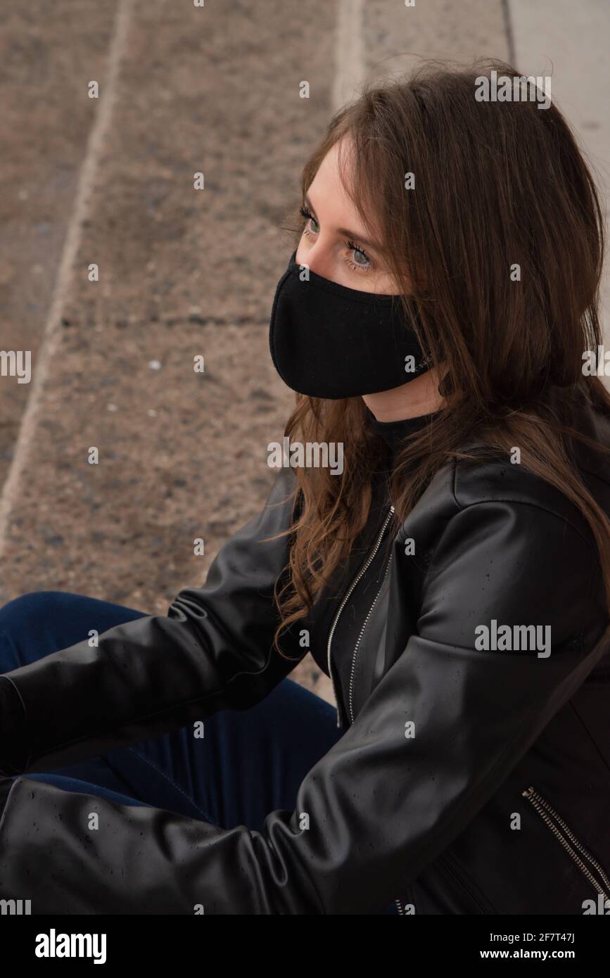 Vertical shot of a Spanish female in black wearing a face mask outdoors ...
