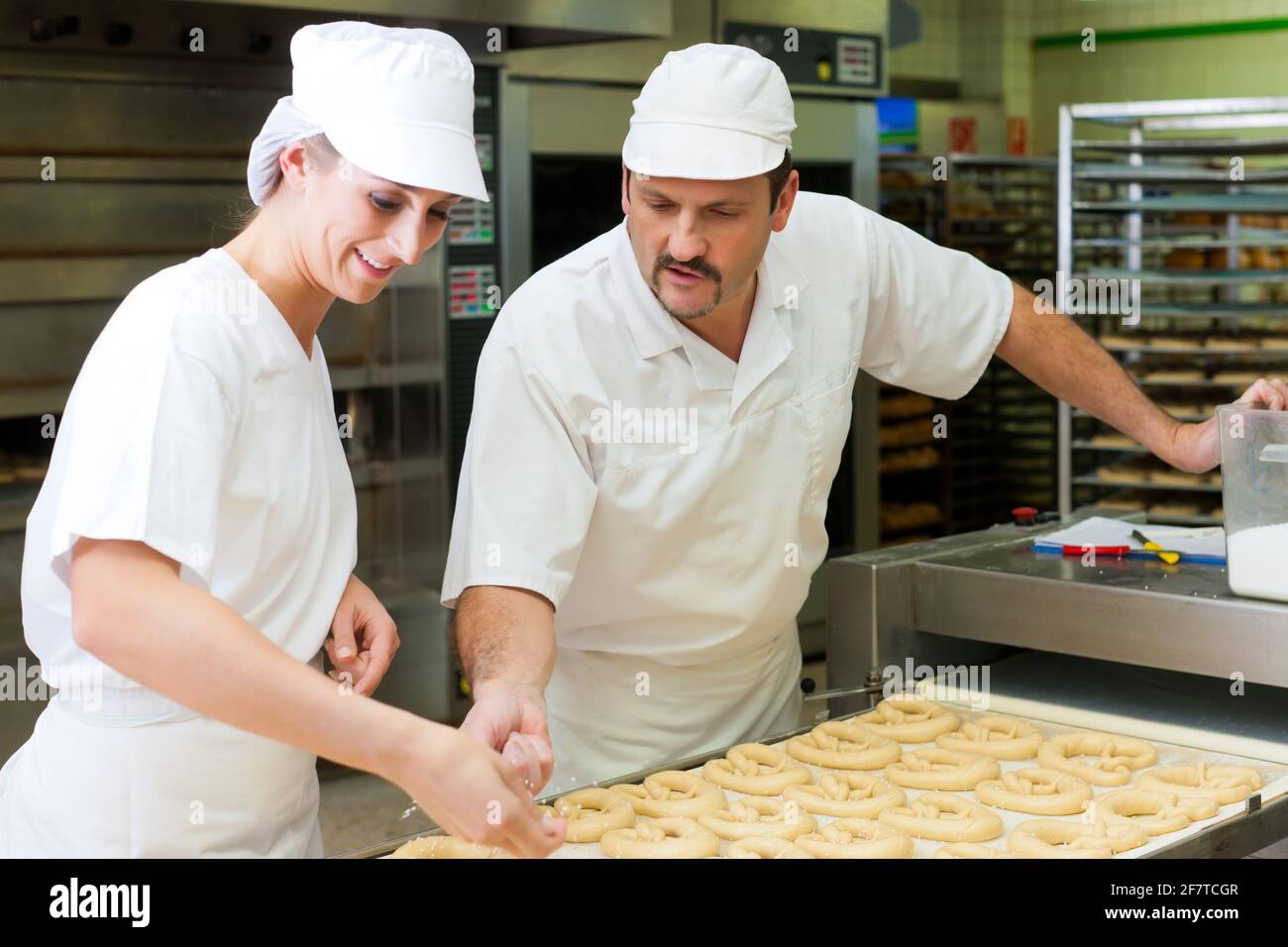 Female and male baker baking fresh bread in the bakehouse, they produce ...