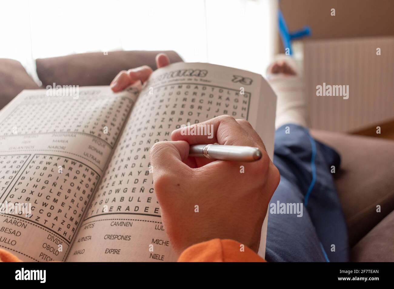 Closeup shot of a man with his leg in a cast working on word search ...