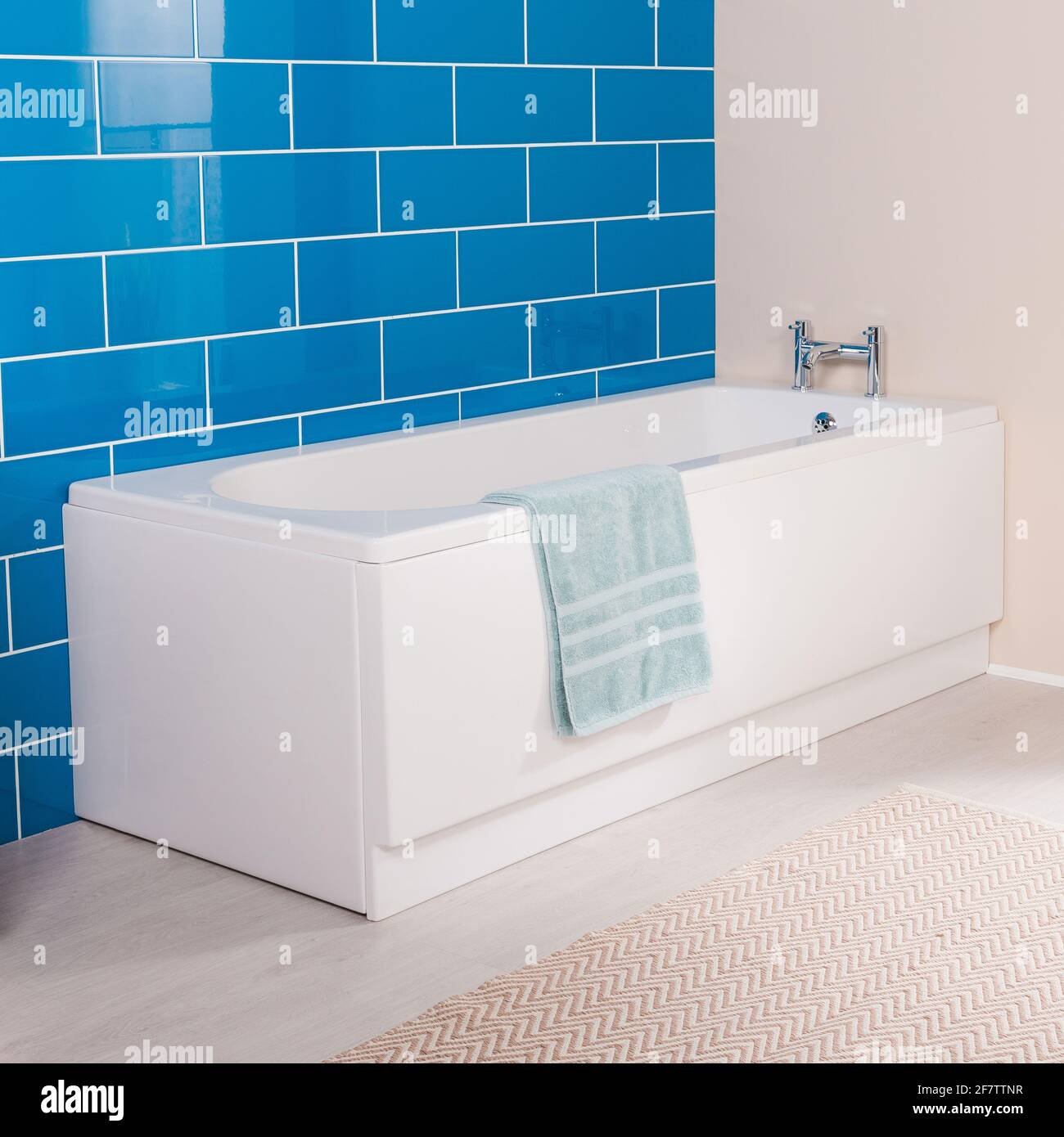 Angled side view of a sleek modern bathtub next to a blue brick wall in ...