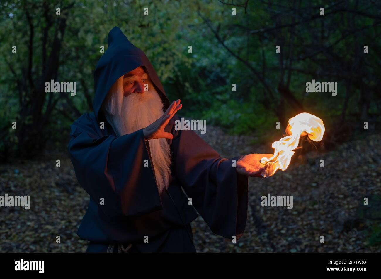 An elderly gray-haired witcher casts a fire spell in the forest. Man in ...