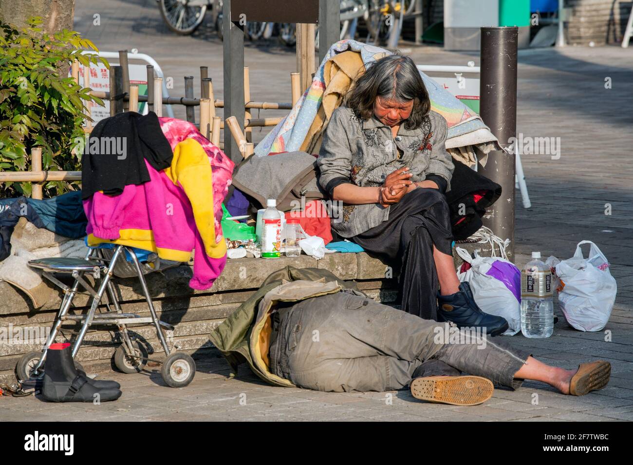 Homeless Japanese female sat smoking cigarette on brick wall, with ...