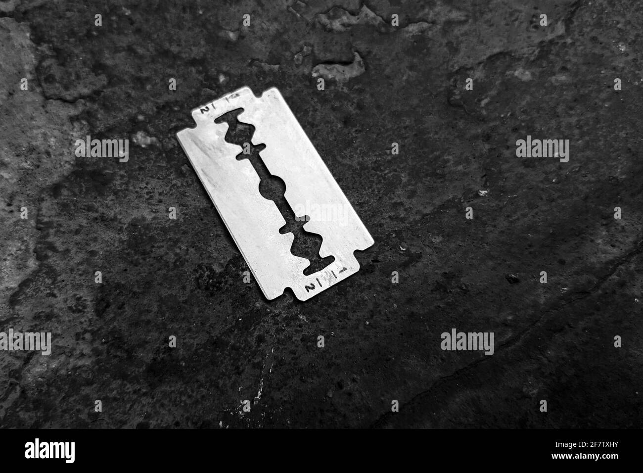 Closeup grayscale of a steel sharp shaving razor blade on the ground ...