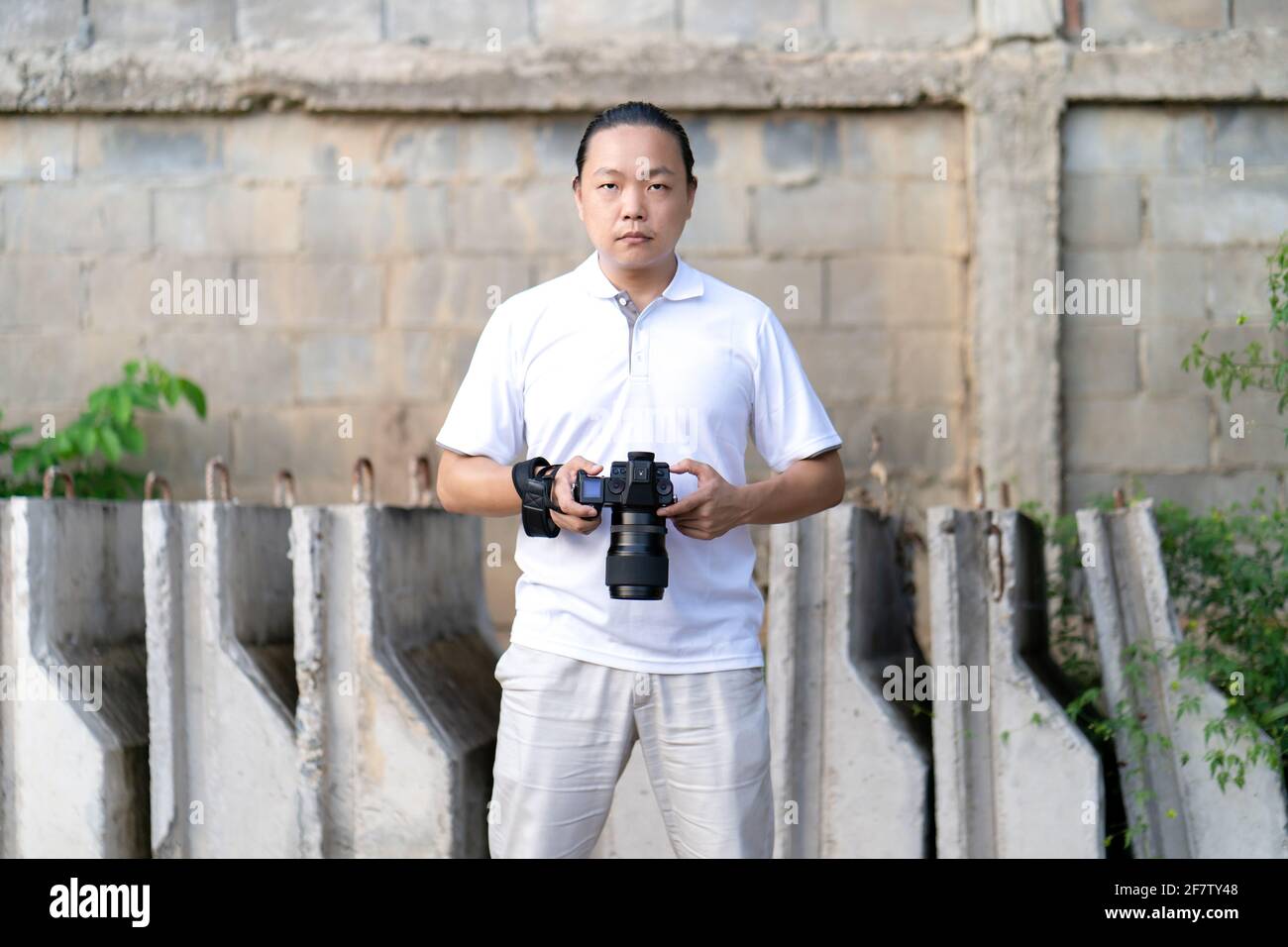 Asian man serious looks at the camera while holds th mirrorless camera ...
