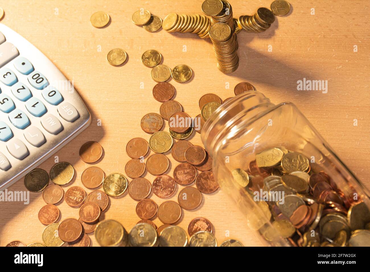 Top view of a half empty jar of coins with coin piles and more coins on ...