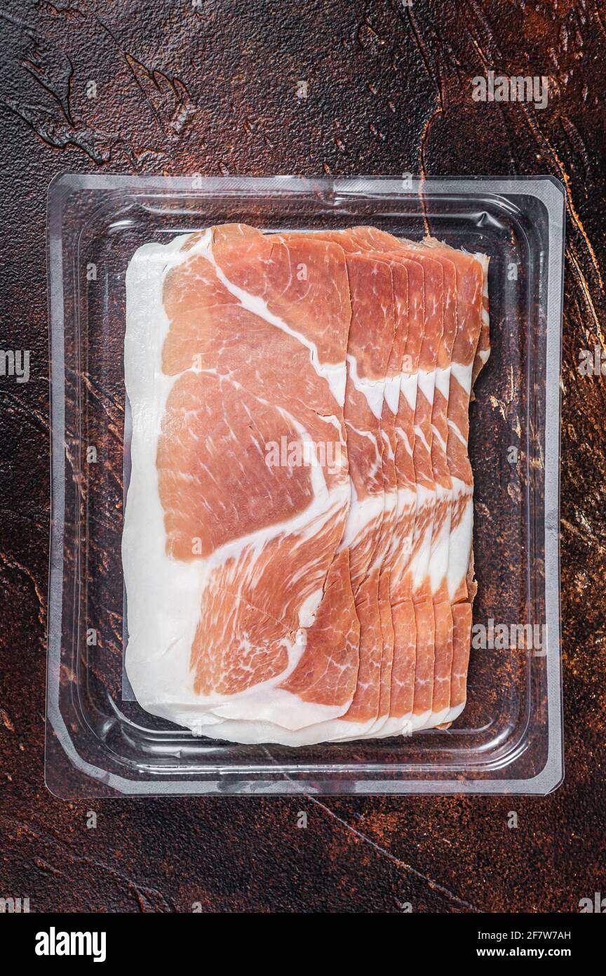 Italian prosciutto crudo or jamon in a vacuum package. Dark background ...