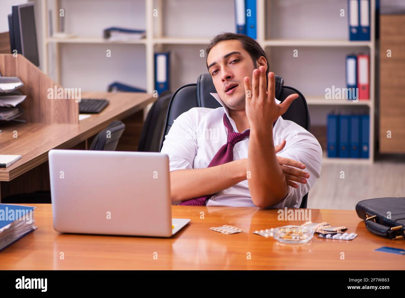 Young drug addicted male employee sitting at workplace Stock Photo - Alamy