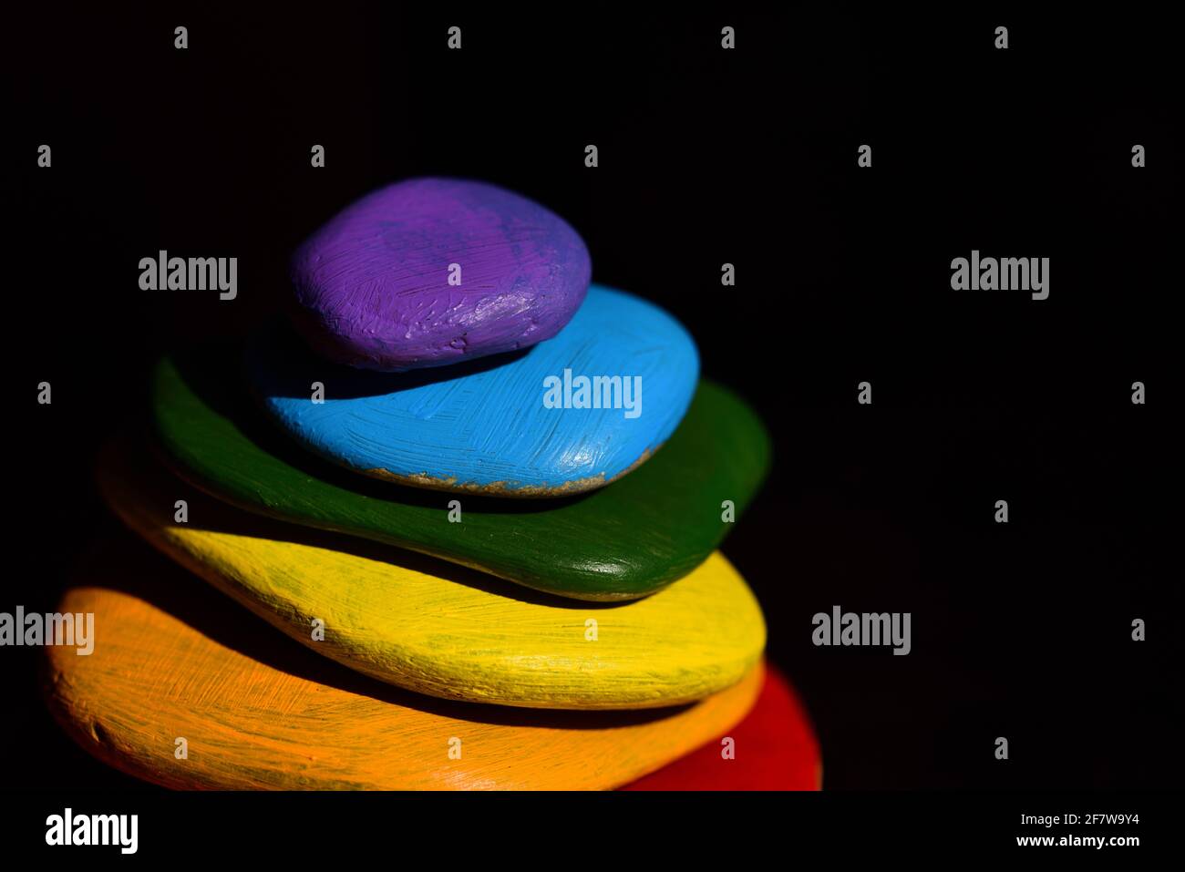 Several brightly colored pebbles painted in rainbow colors lie on top ...