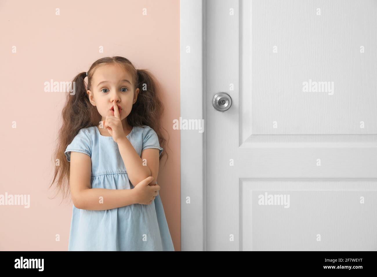 Cute little girl showing silence gesture near closed door Stock Photo ...