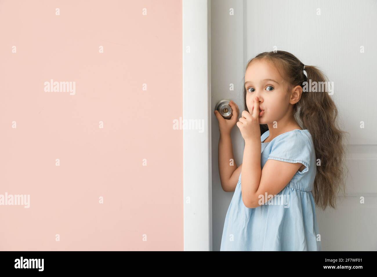 Cute little girl showing silence gesture near closed door Stock Photo ...