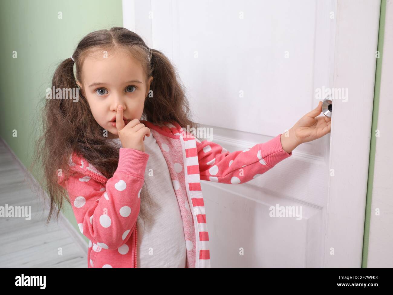Cute little girl showing silence gesture near closed door Stock Photo ...