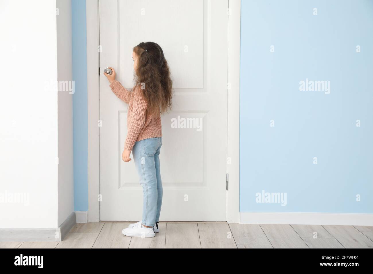 Cute little girl standing near closed door Stock Photo - Alamy